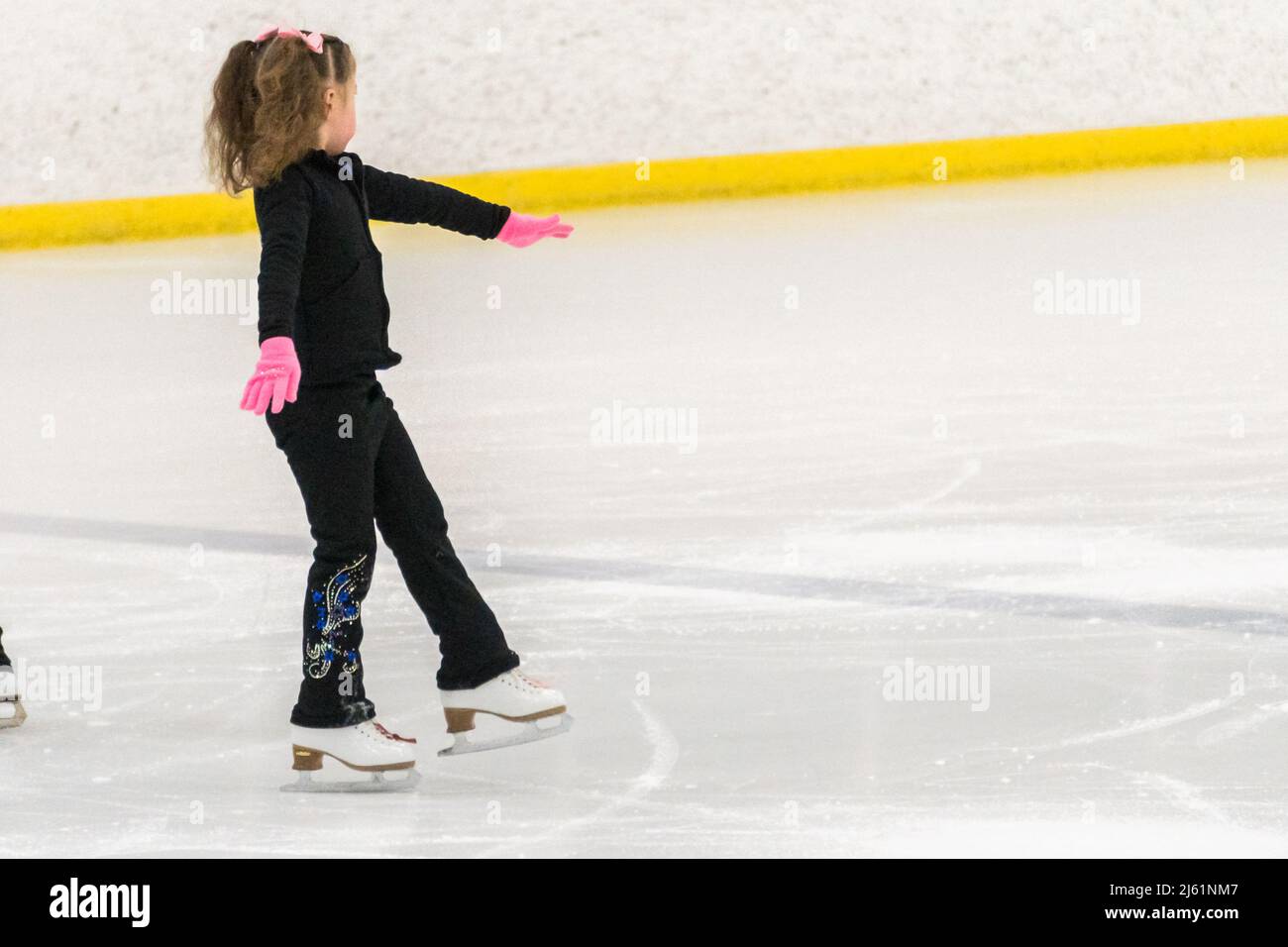 Little girl practicing figure skating moves on the indoor ice rink ...