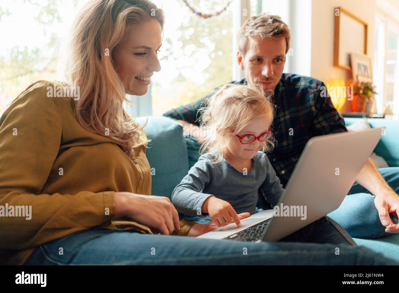 Little girl using laptop sitting with parents on sofa at home Stock ...