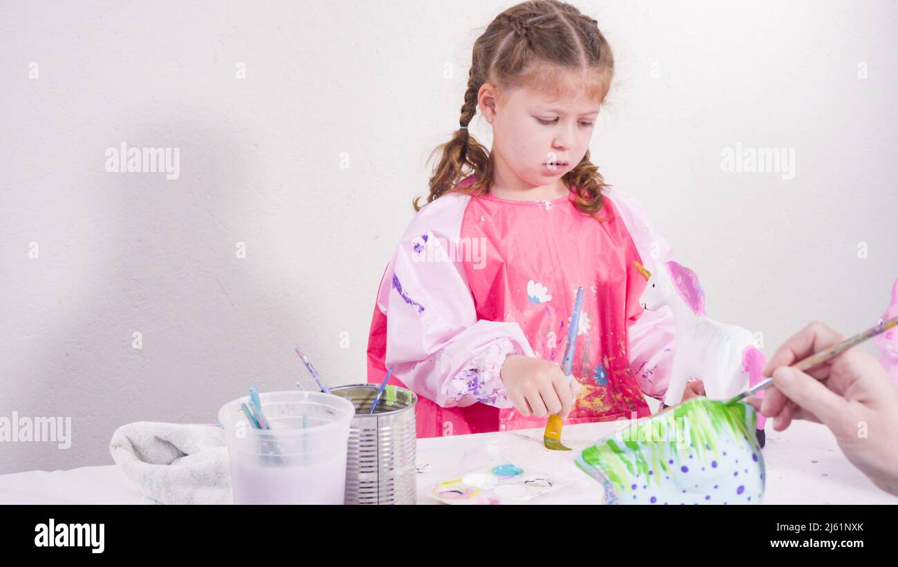 Little girl painting paper mache figurines with acrylic paint for her ...