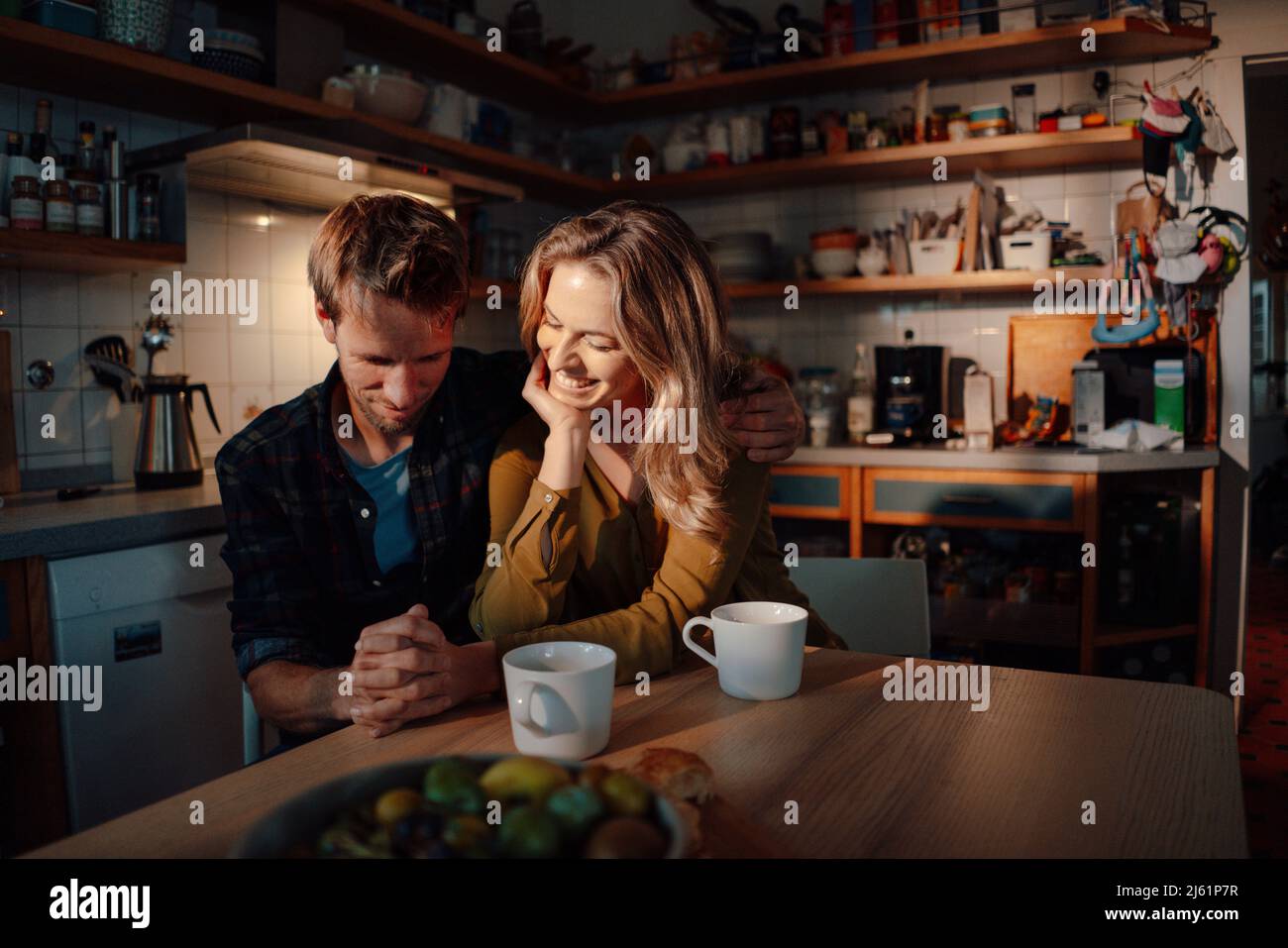 Couple holding hands sitting at dining table in kitchen Stock Photo - Alamy