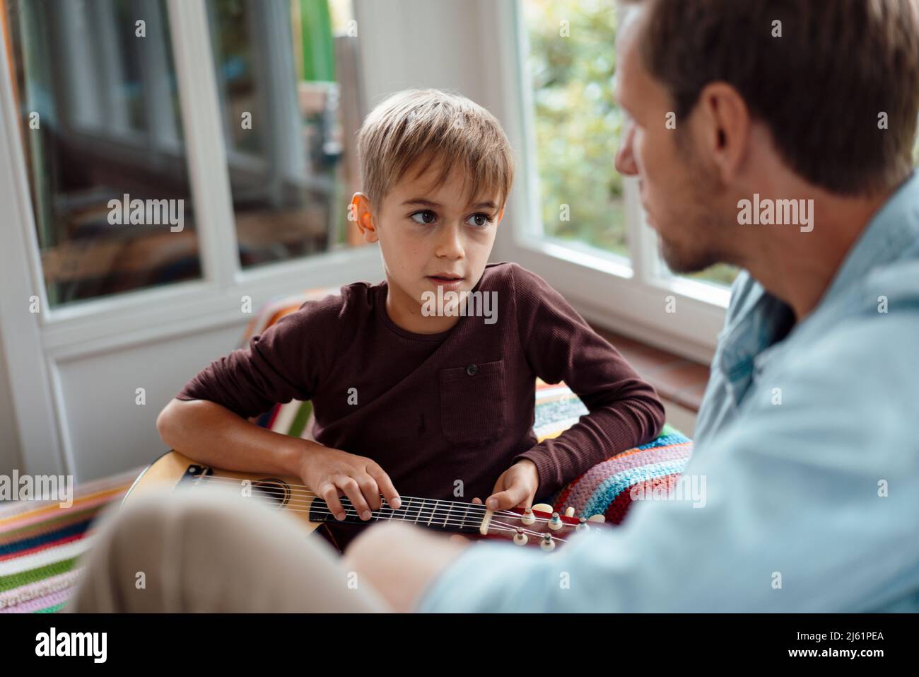 Blond boy with guitar talking with father at home Stock Photo - Alamy