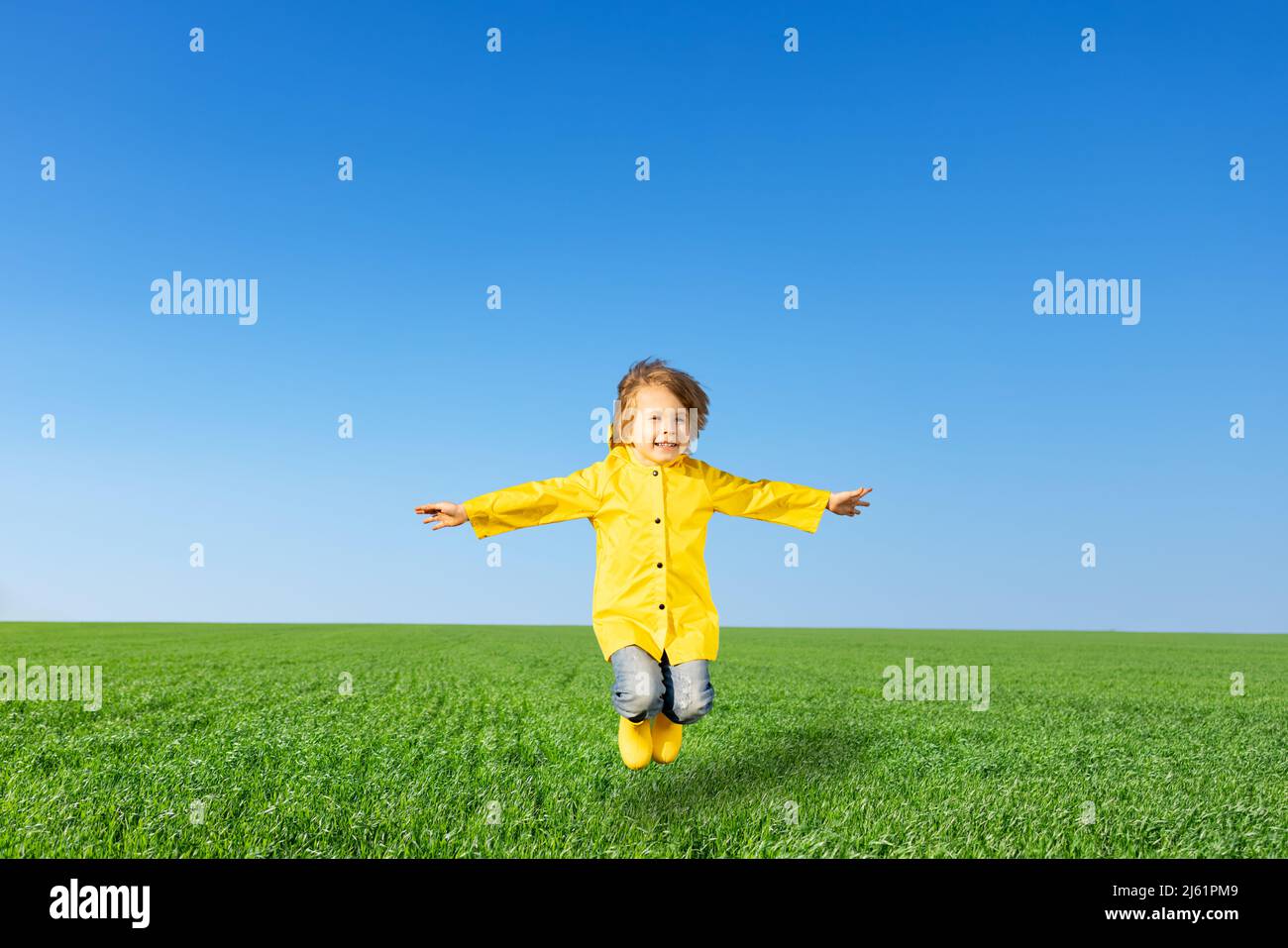 Happy child jumping in green spring field. Kid having fun against blue ...