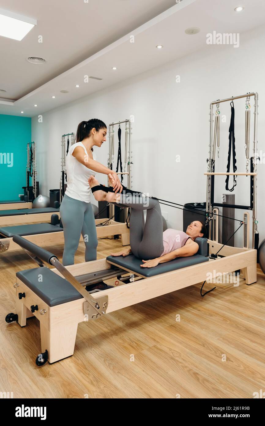 Fitness instructor teaching woman leg exercise at pilates studio Stock ...