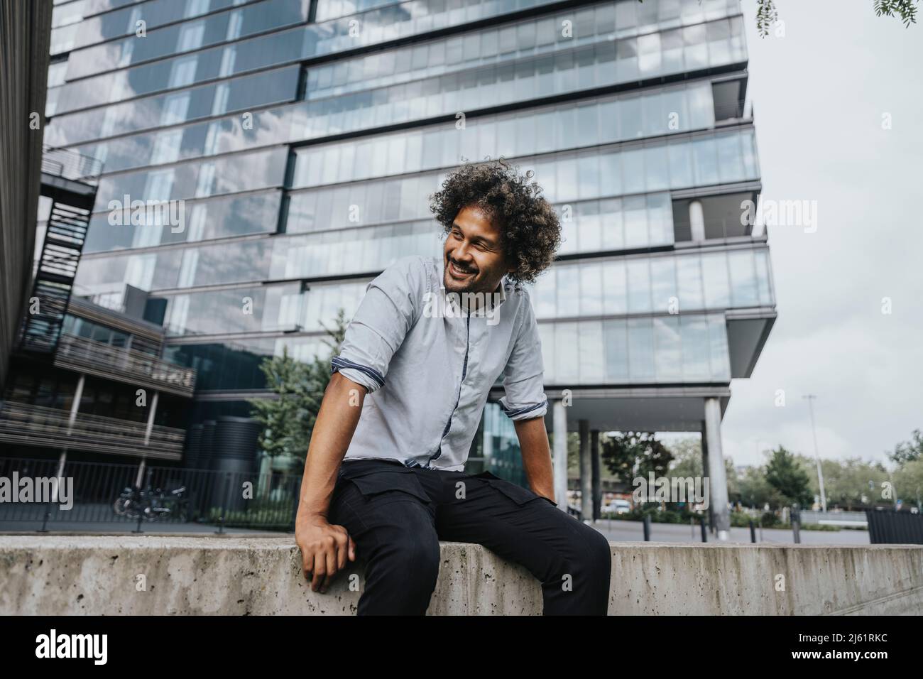 Young man sitting on ledge in front of modern building Stock Photo - Alamy
