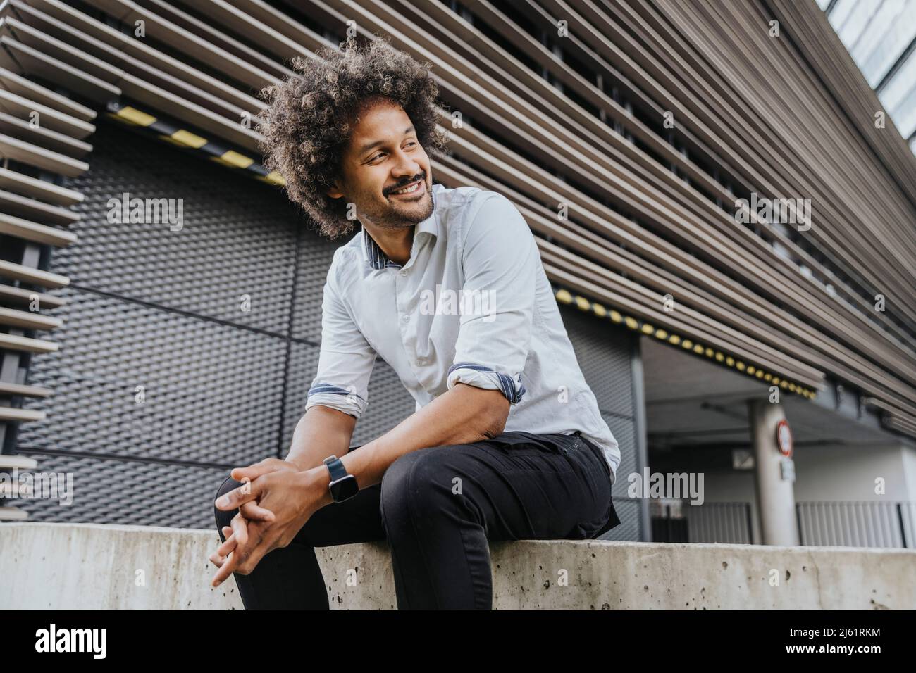 Smiling man sitting on ledge in front of modern building Stock Photo ...