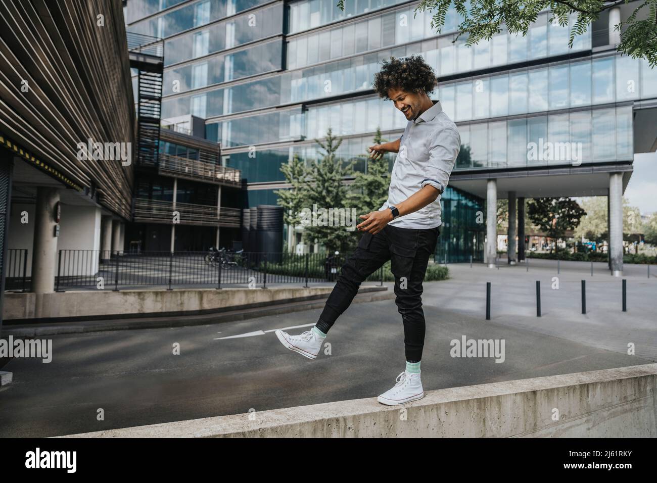 Playful young man balancing on ledge by modern buildings Stock Photo ...