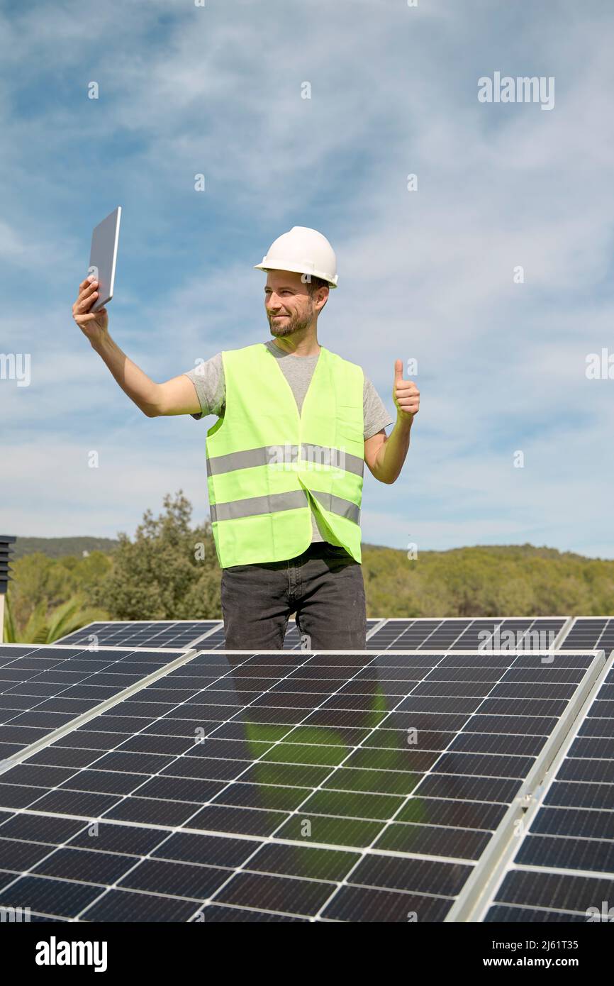 Engineer taking selfie with thumbs up amidst solar panels on rooftop ...