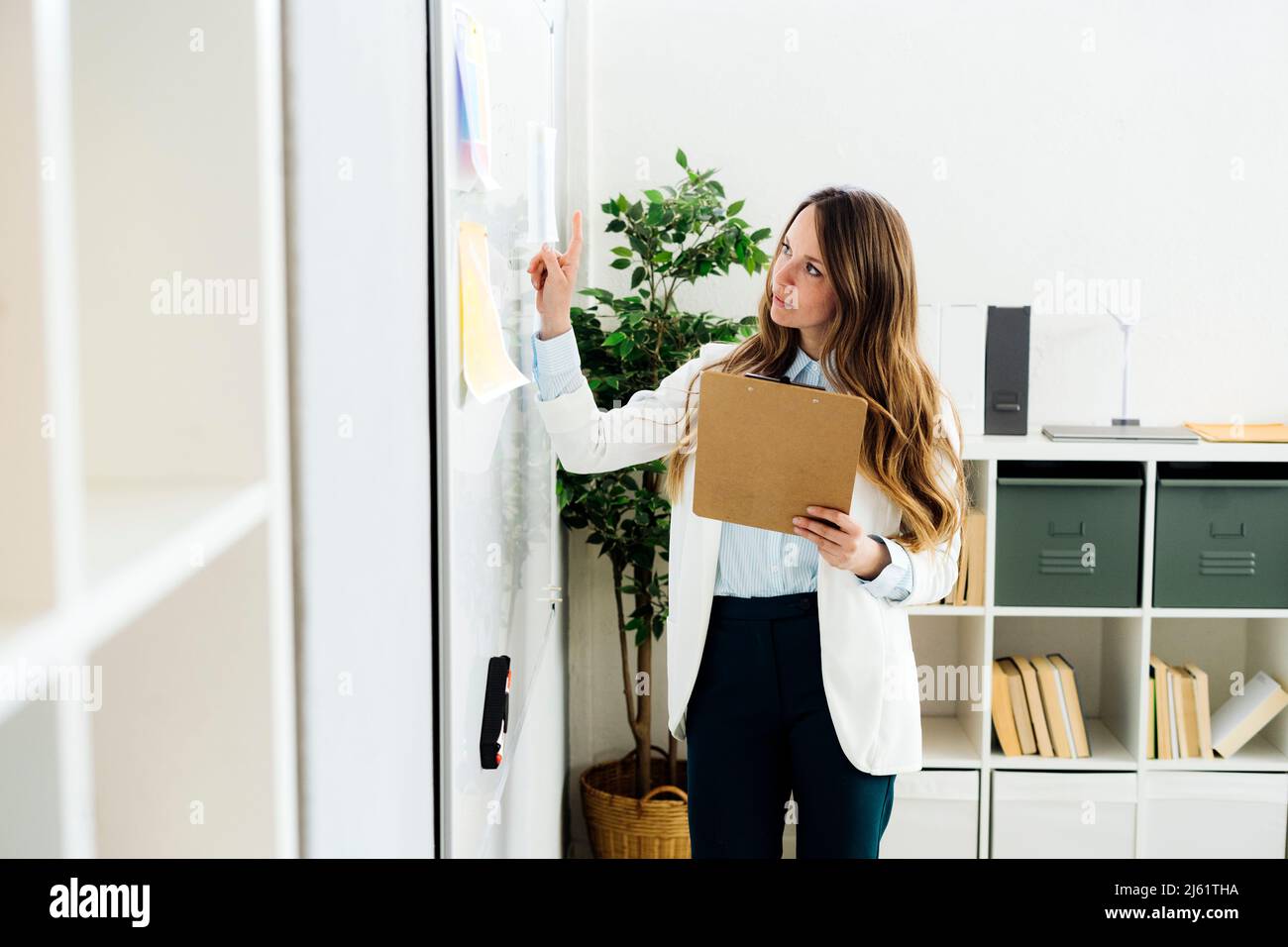Businesswoman holding file folder examining chart on whiteboard in ...