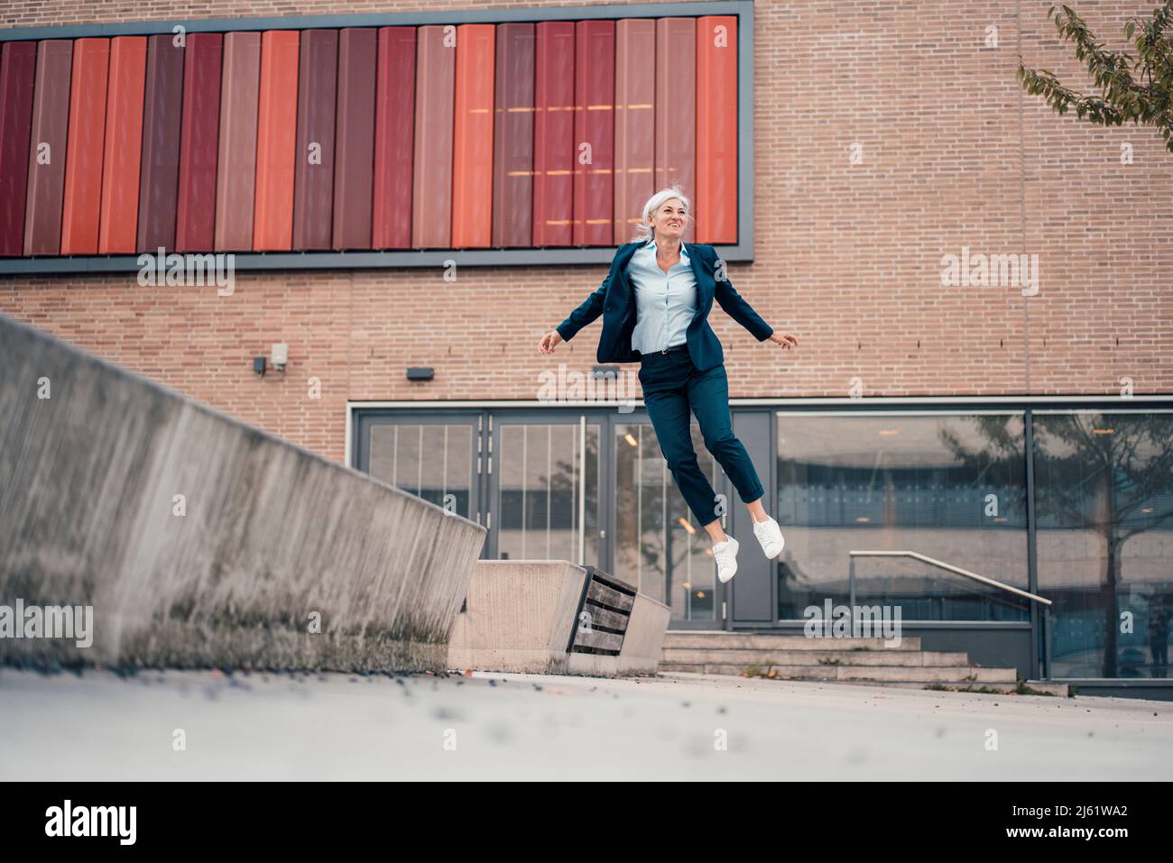 Businesswoman jumping in front of office building Stock Photo - Alamy