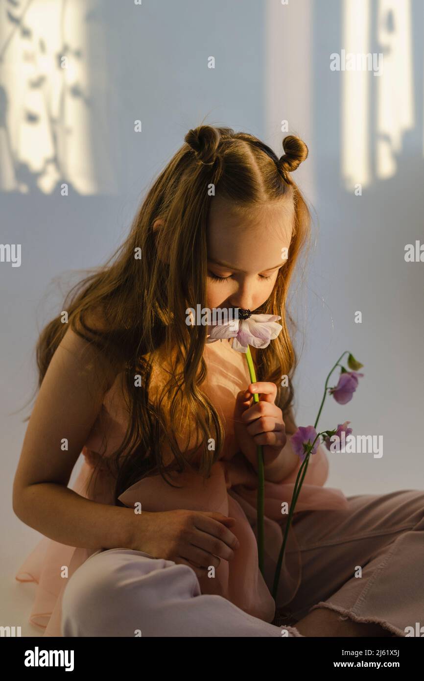 Girl smelling fresh flowers sitting in front of white wall Stock Photo ...