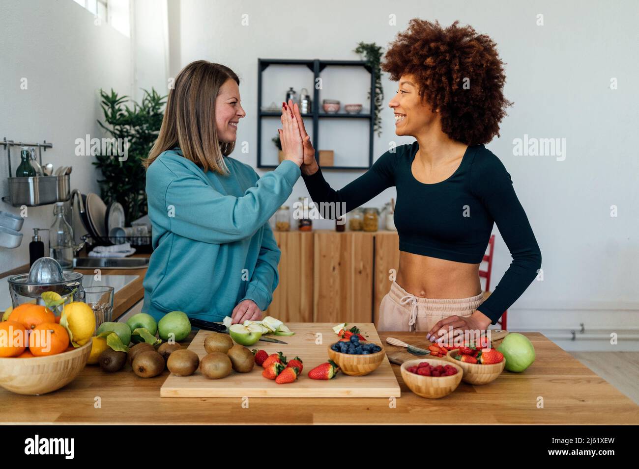 Happy friends giving high-five to each other standing in kitchen at ...