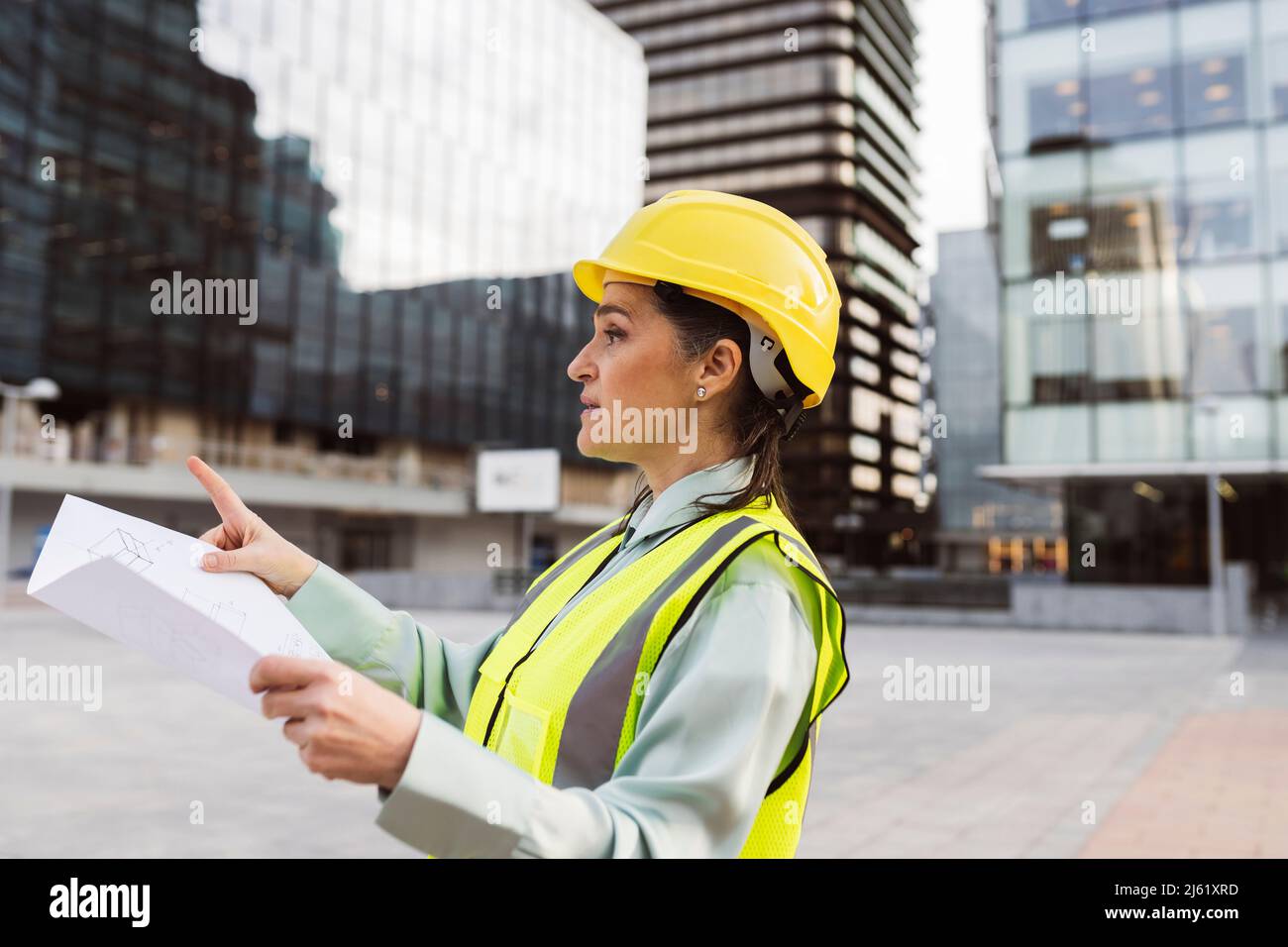 Engineer wearing hardhat holding blueprint working outside modern ...
