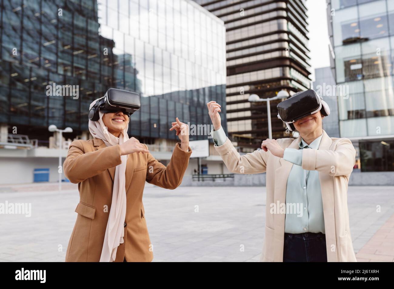 Smiling businesswomen wearing virtual reality simulator gesturing ...