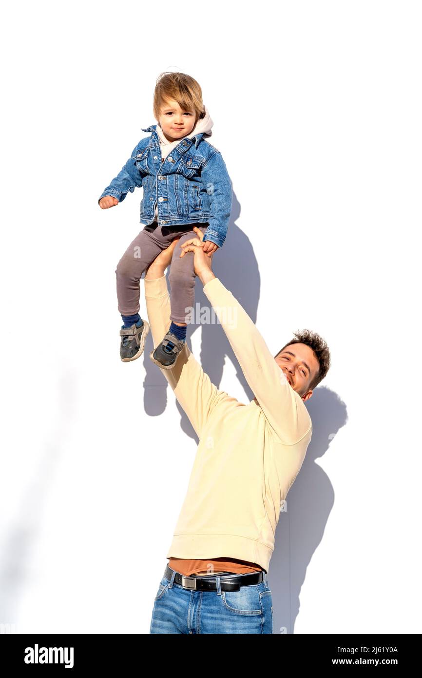 Playful man lifting son on hand standing in front of white wall Stock ...