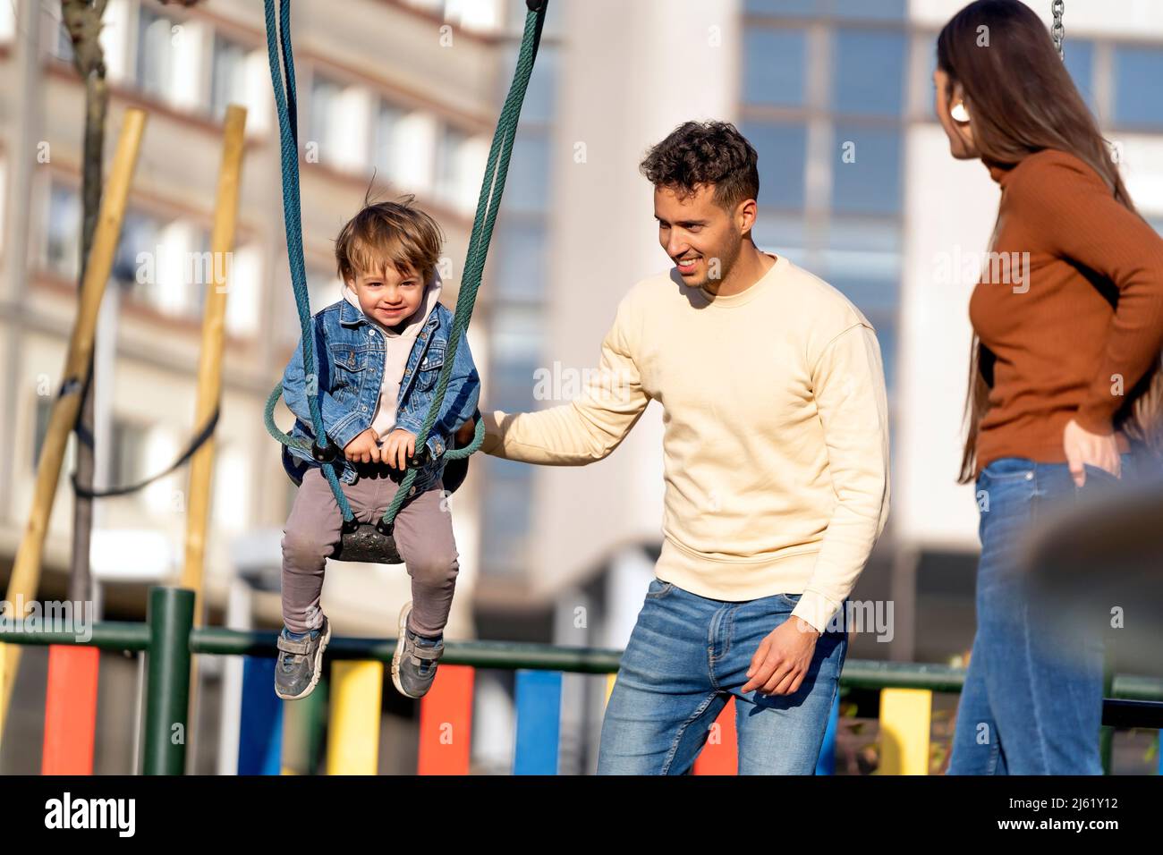 Smiling man pushing son on swing standing by woman in playground Stock ...