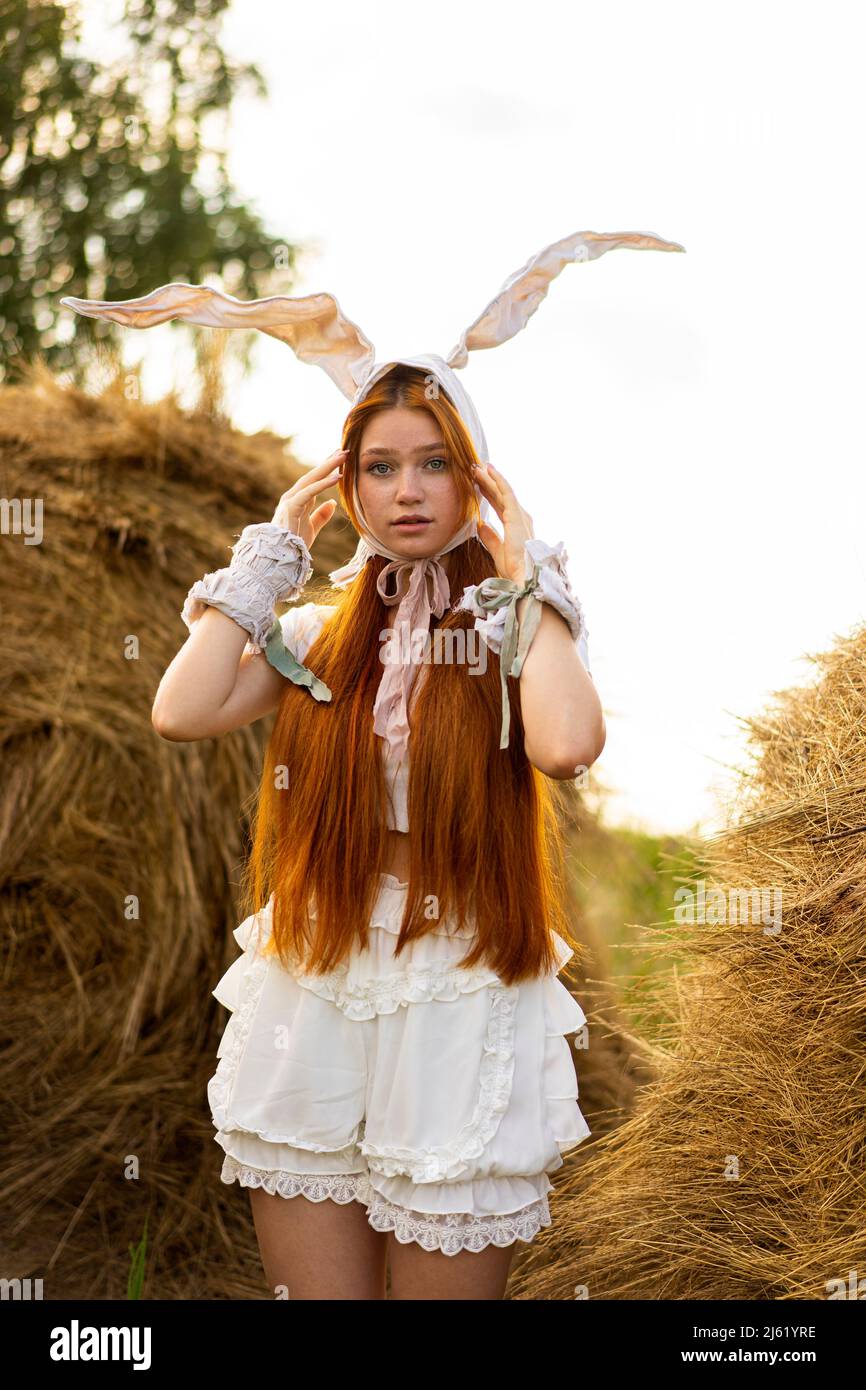 Young redhead woman adjusting rabbit costume ears standing at farm ...