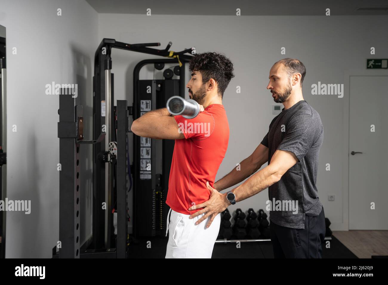 Instructor giving support to young man lifting barbell at gym Stock ...
