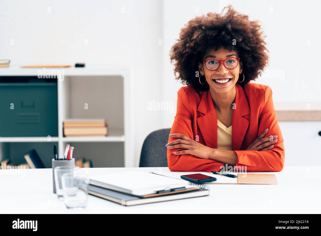 Smiling businesswoman wearing eyeglasses sitting with arms crossed at ...