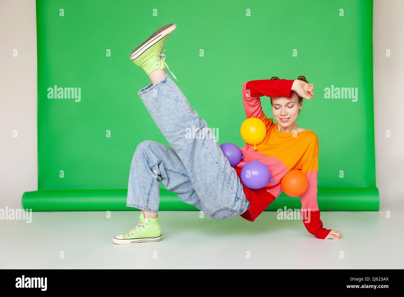 Smiling woman with colorful balloons balancing on leg against green ...