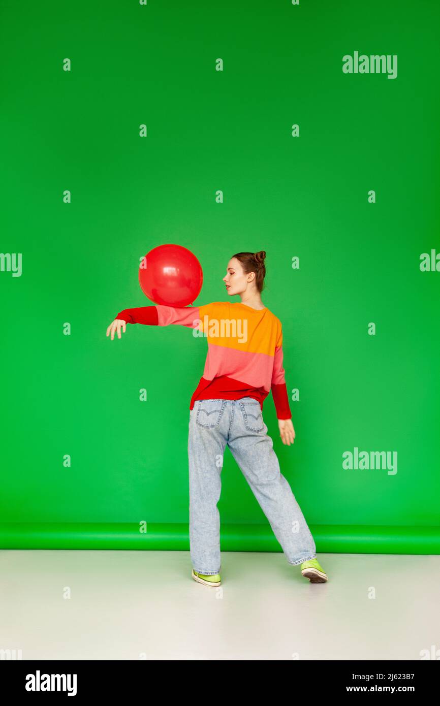 Woman balancing red balloon on arm against green background Stock Photo ...