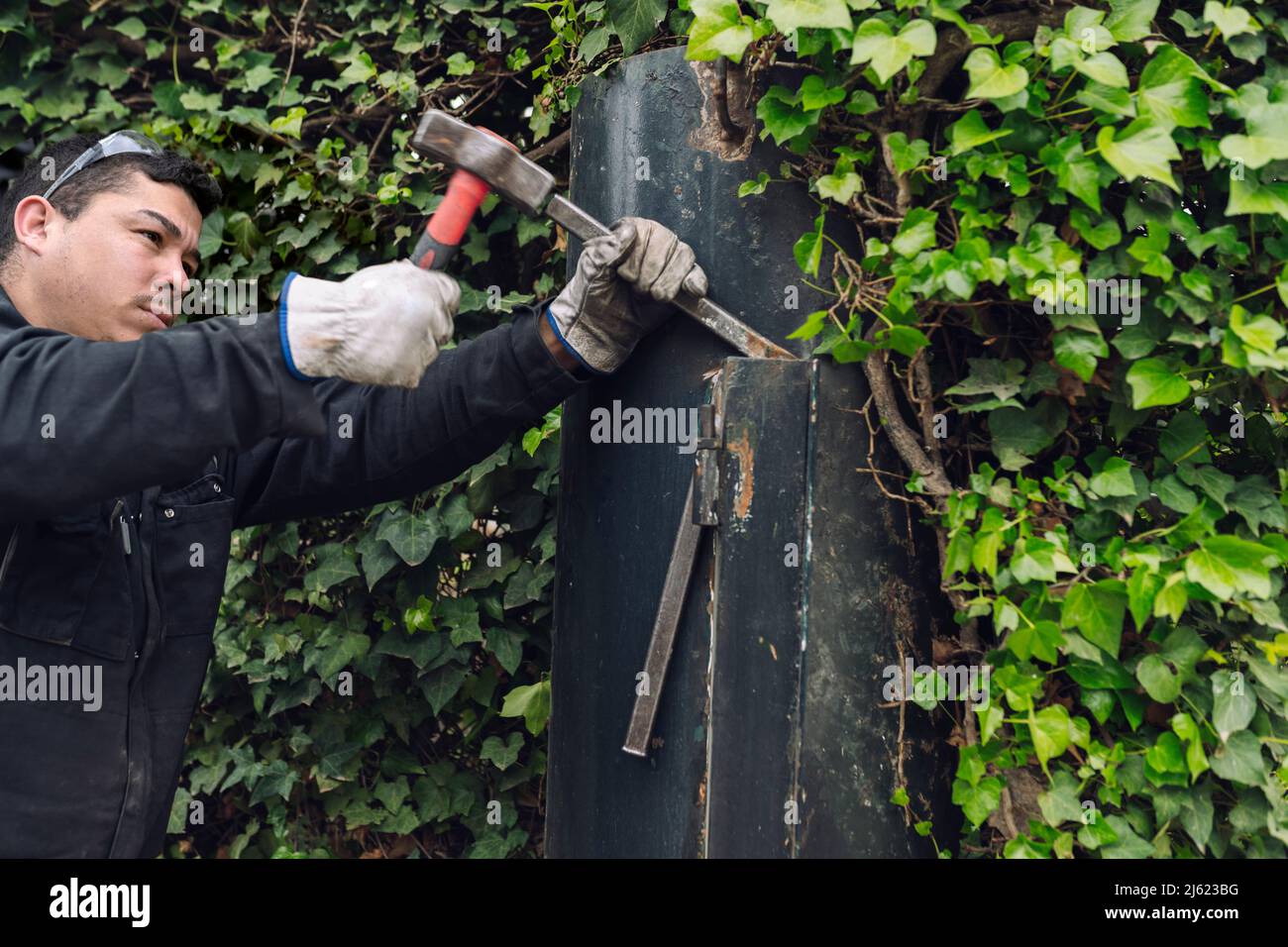 Construction worker with hammer working on metal gate Stock Photo - Alamy
