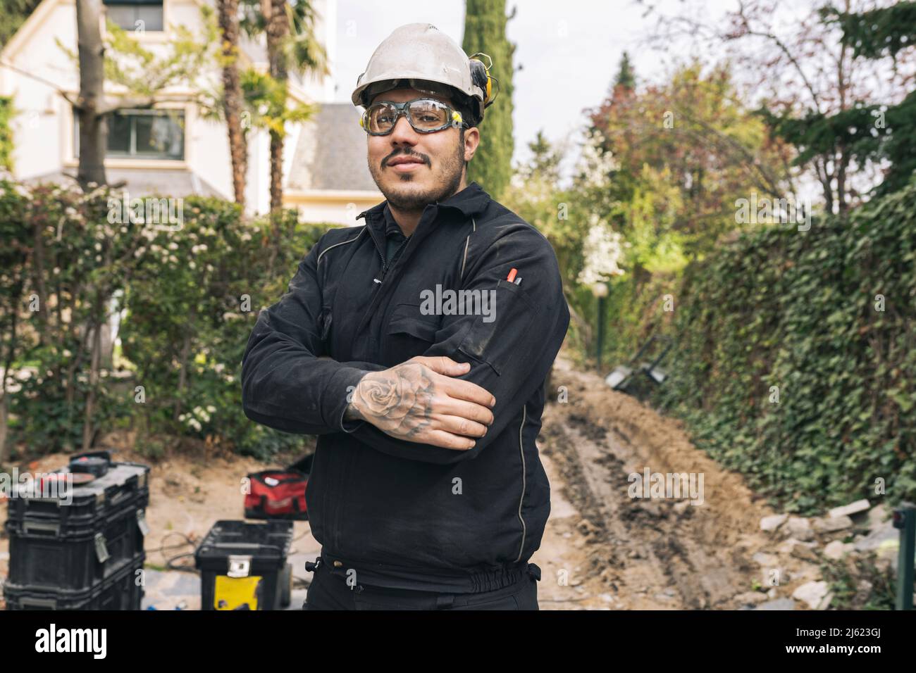 Smiling construction worker standing with arms crossed at construction ...