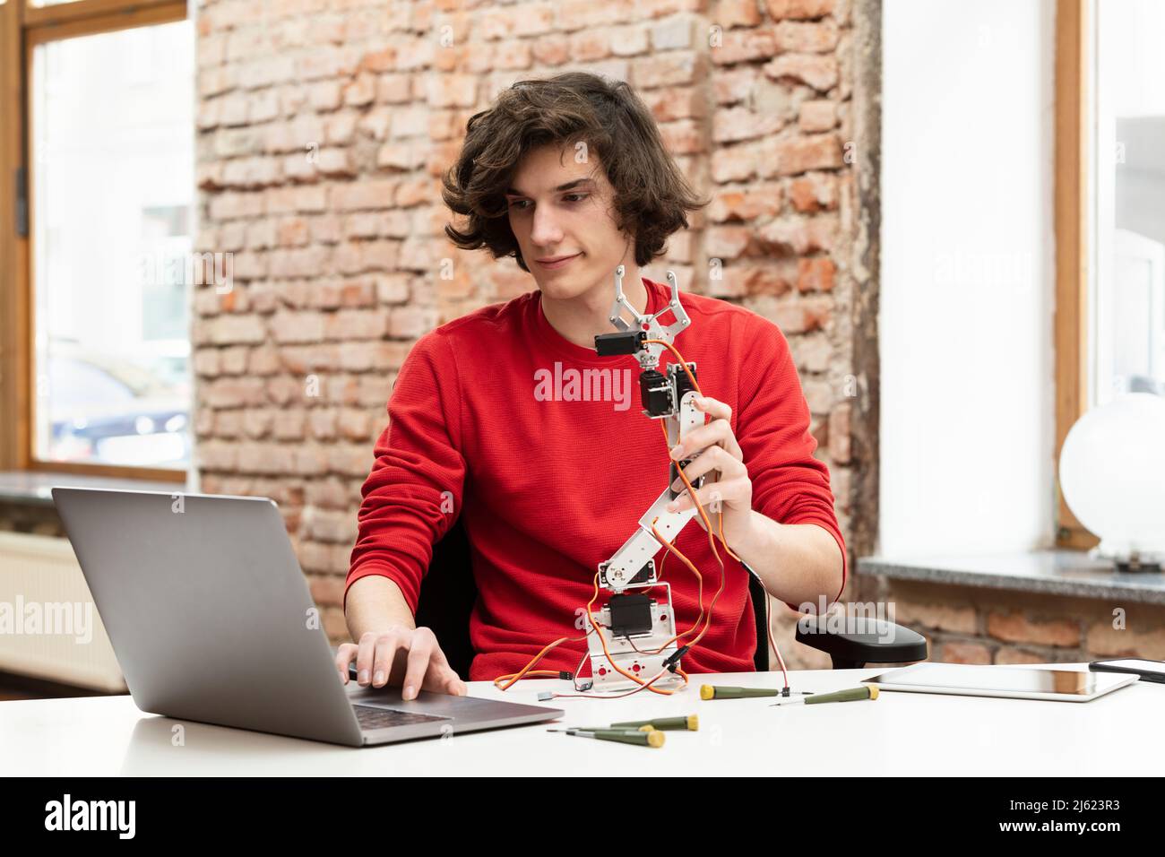 Smiling teenage boy with robotic arm using laptop sitting at table ...