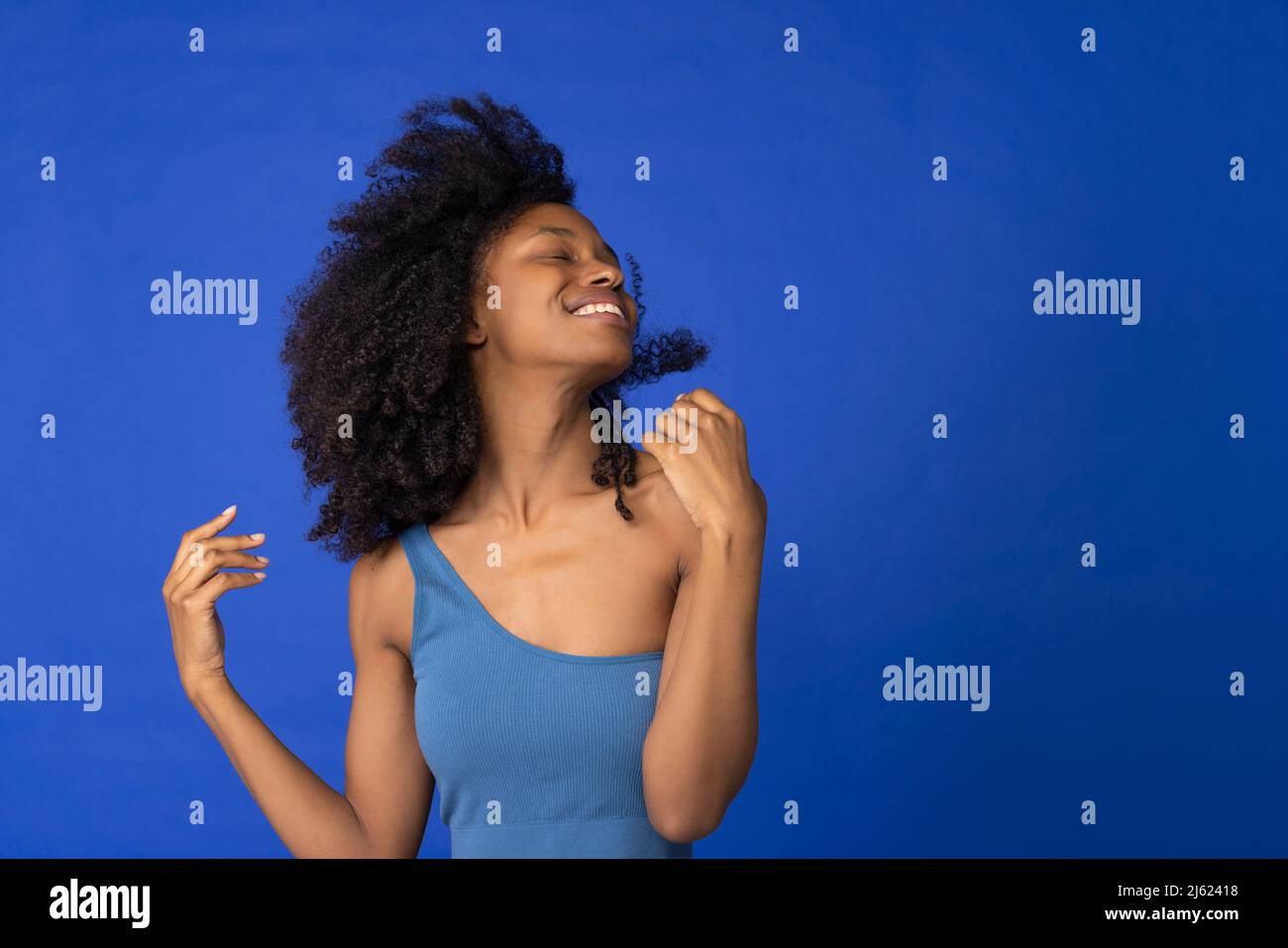 Happy young woman with eyes closed dancing against blue background ...