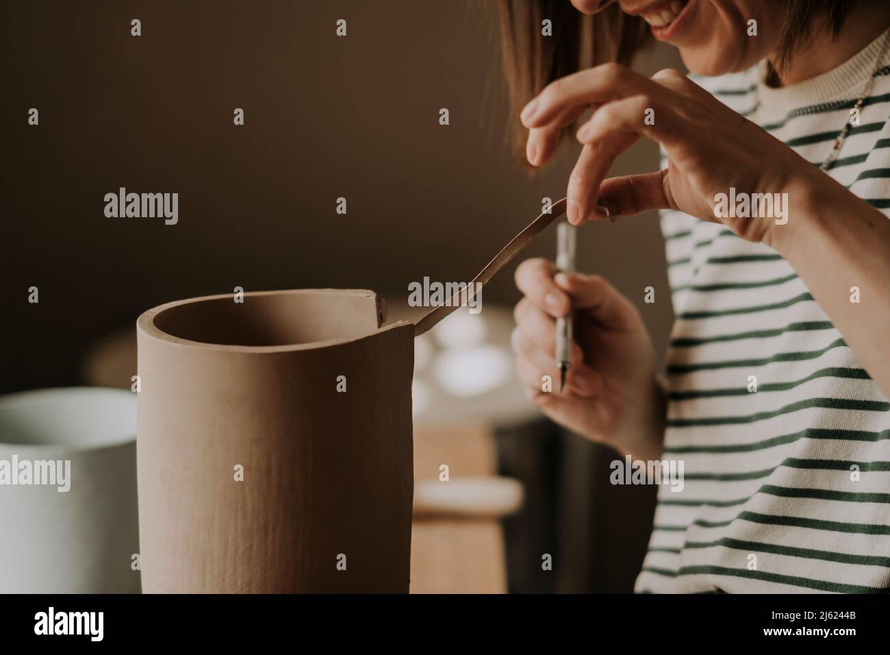 Craftsperson cutting excess clay of pot with hand tool at workshop ...