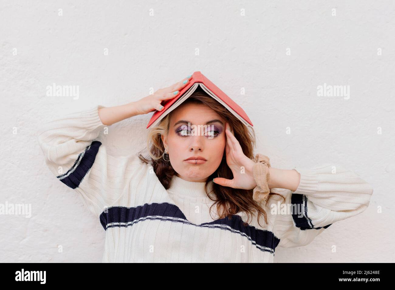 Bored young woman carrying book on head in front of white wall Stock ...