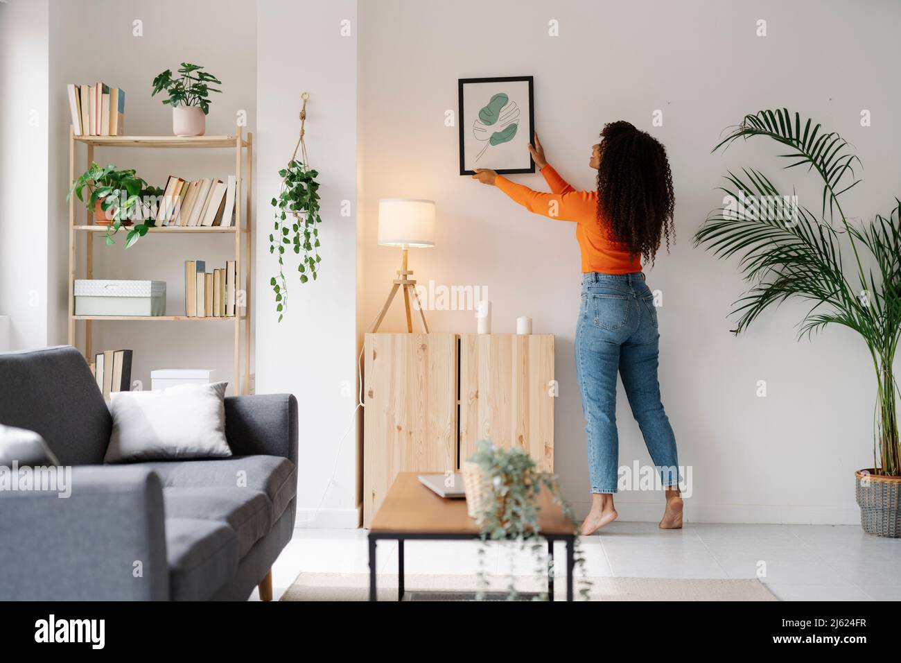 Young woman hanging picture frame on wall in living room at home Stock ...