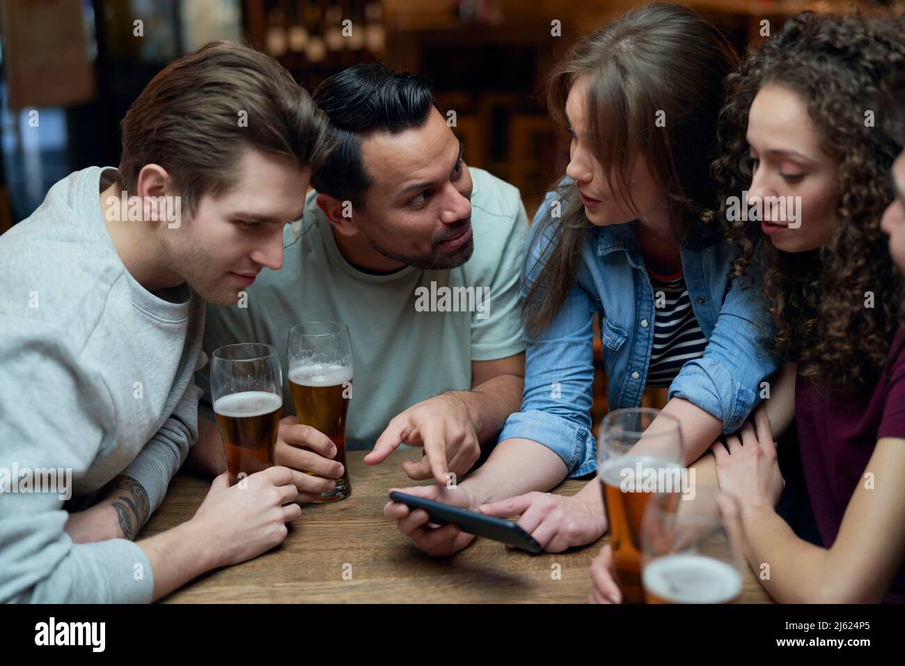 Group of friends having beer and sharing a smartphone in a pub Stock ...