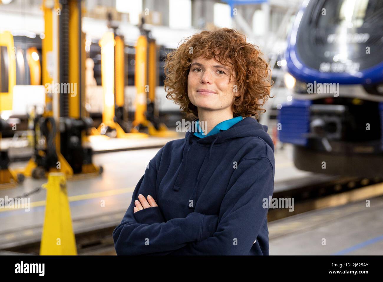 Confident engineer with arms crossed standing in warehouse at factory ...