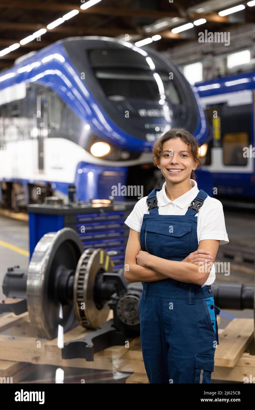 Smiling young trainee standing with arms crossed in warehouse at ...