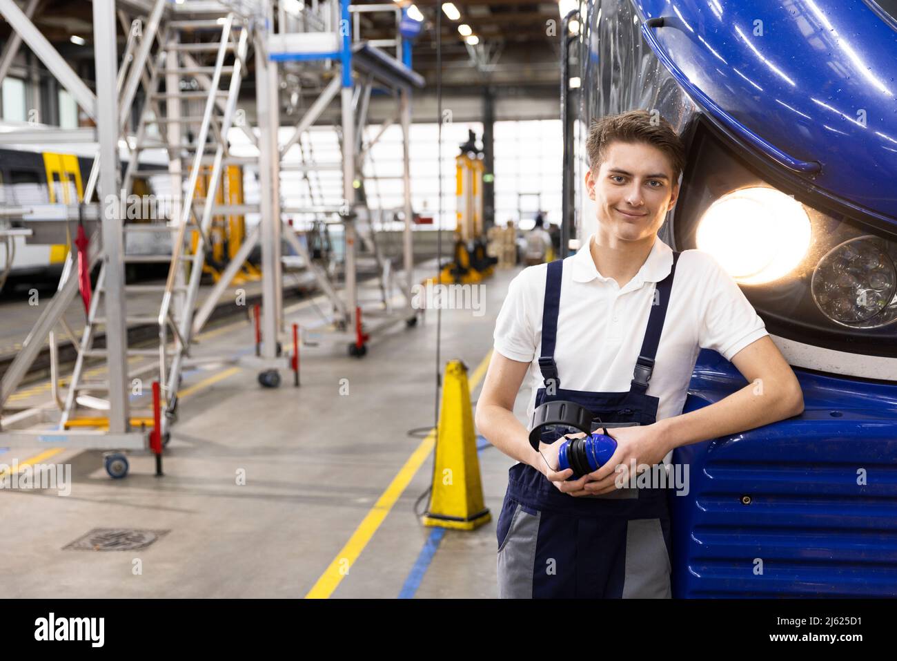 Smiling young trainee standing by monorail in factory Stock Photo - Alamy