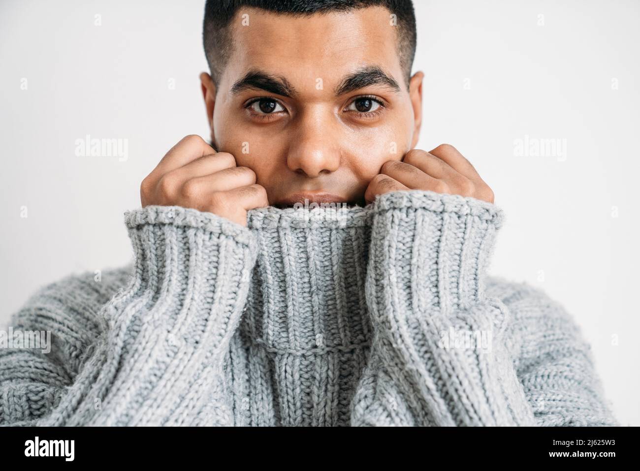 Man covering face with gray woolen sweater against white background ...