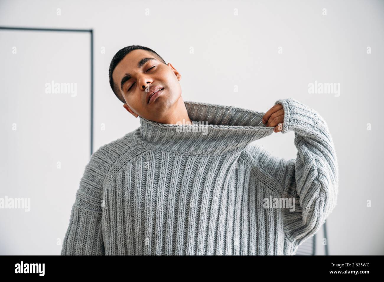 Young man with eyes closed pulling sweater in front of wall Stock Photo ...