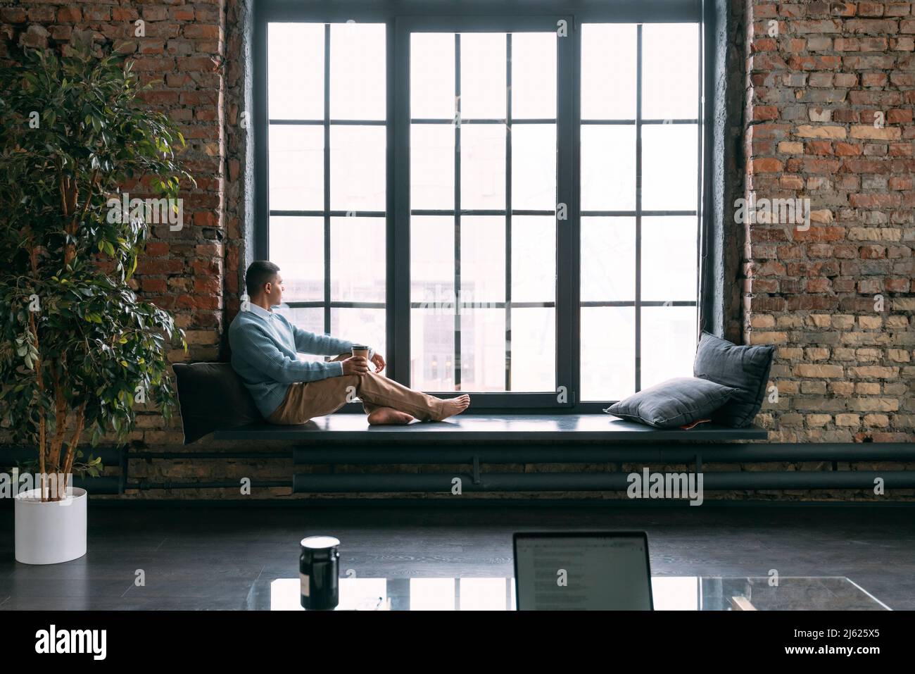 Freelancer with disposable coffee cup sitting on window sill at home ...