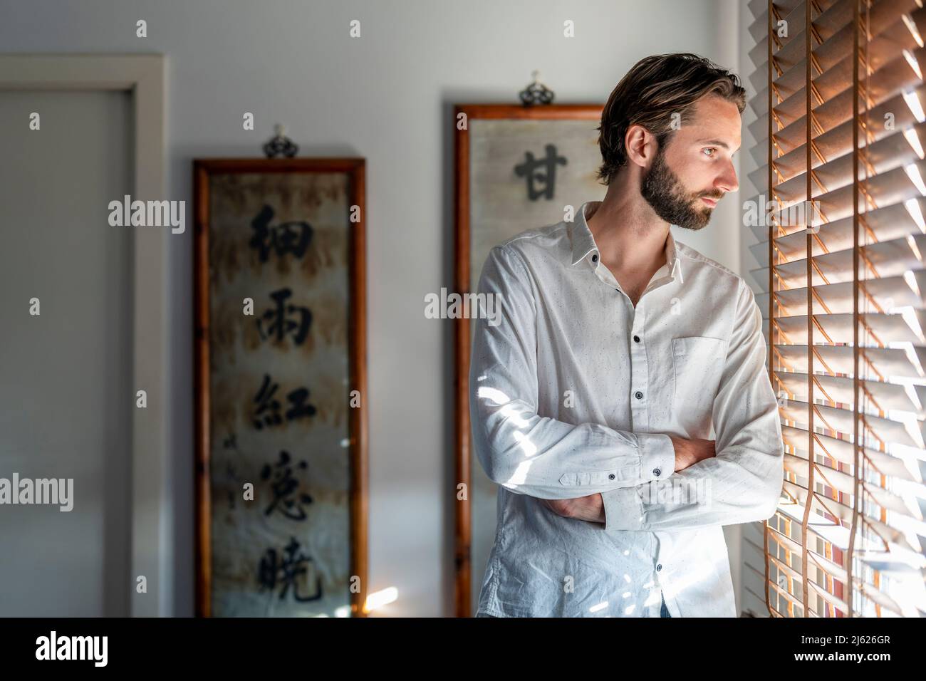 Portrait of man standing by blinded window with arms crossed Stock ...
