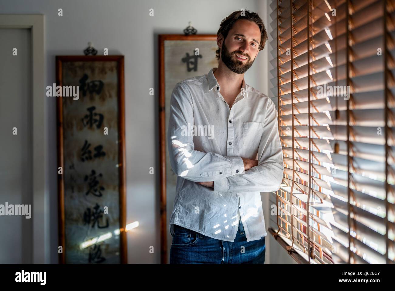Portrait of man standing by blinded window with arms crossed Stock ...