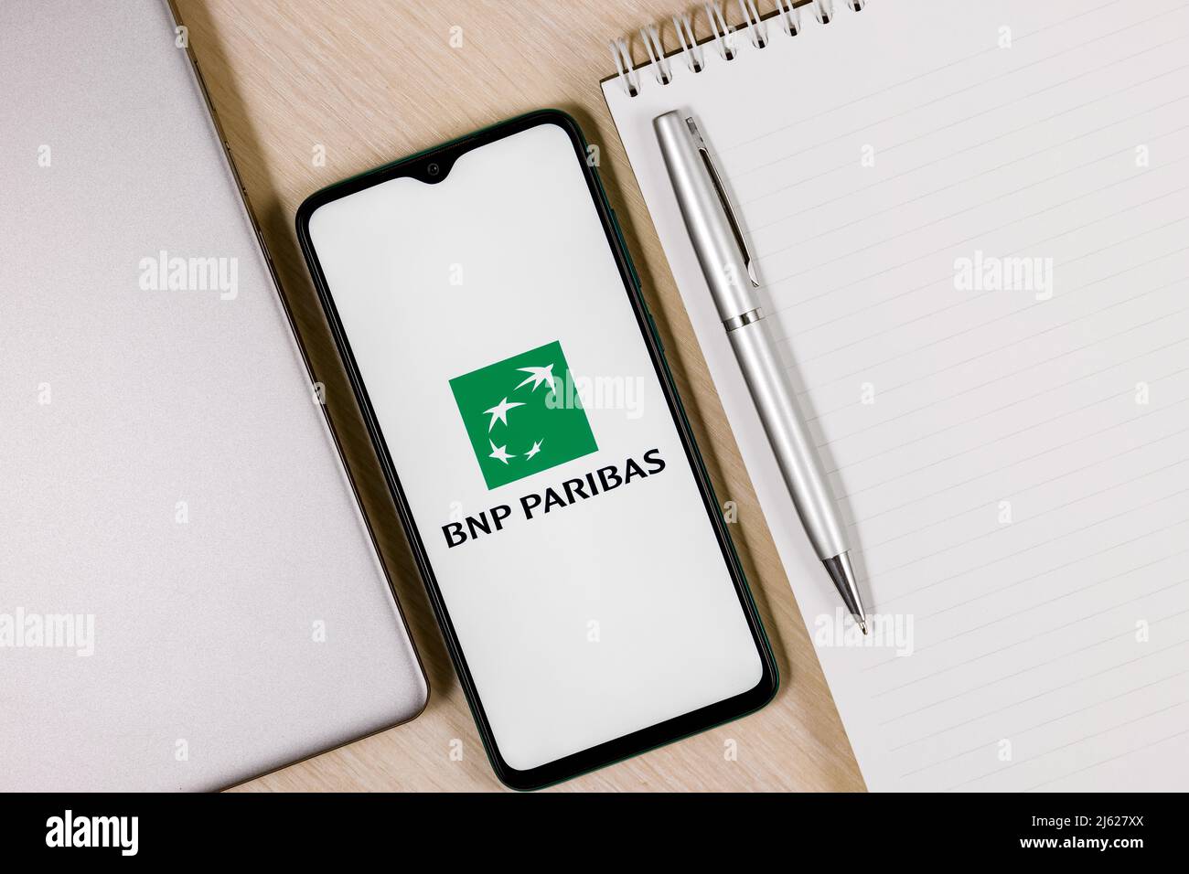 Smartphone with BNP Paribas bank logo on wooden table next to laptop ...