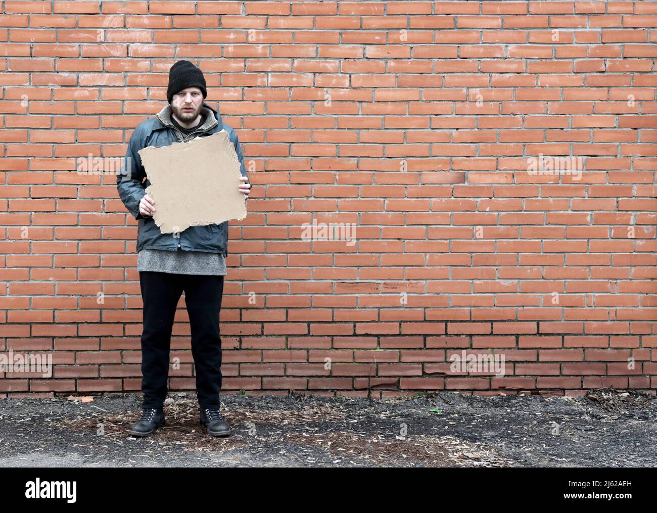Homeless holds piece of cardboard. Refugee is at brick wall looking for ...