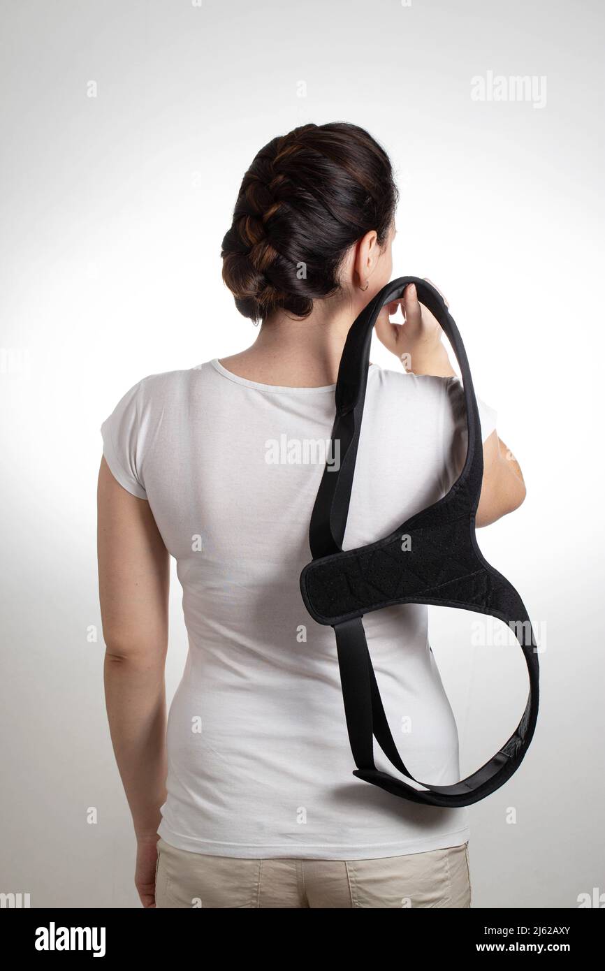 A girl in a white T-shirt wears a posture corrector on a white ...