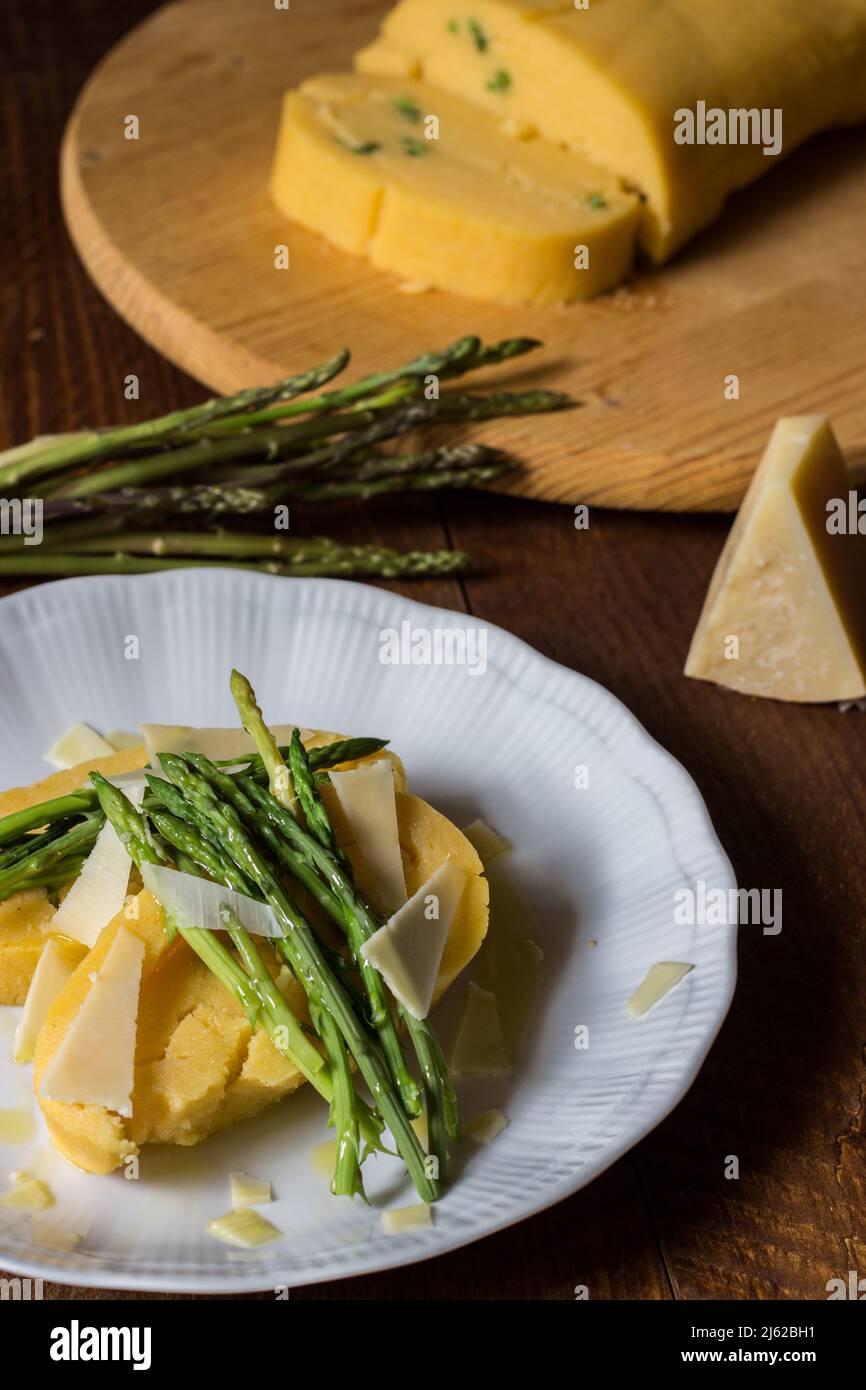 Rolled corn porridge with asparagus and cheese flakes on white plate ...