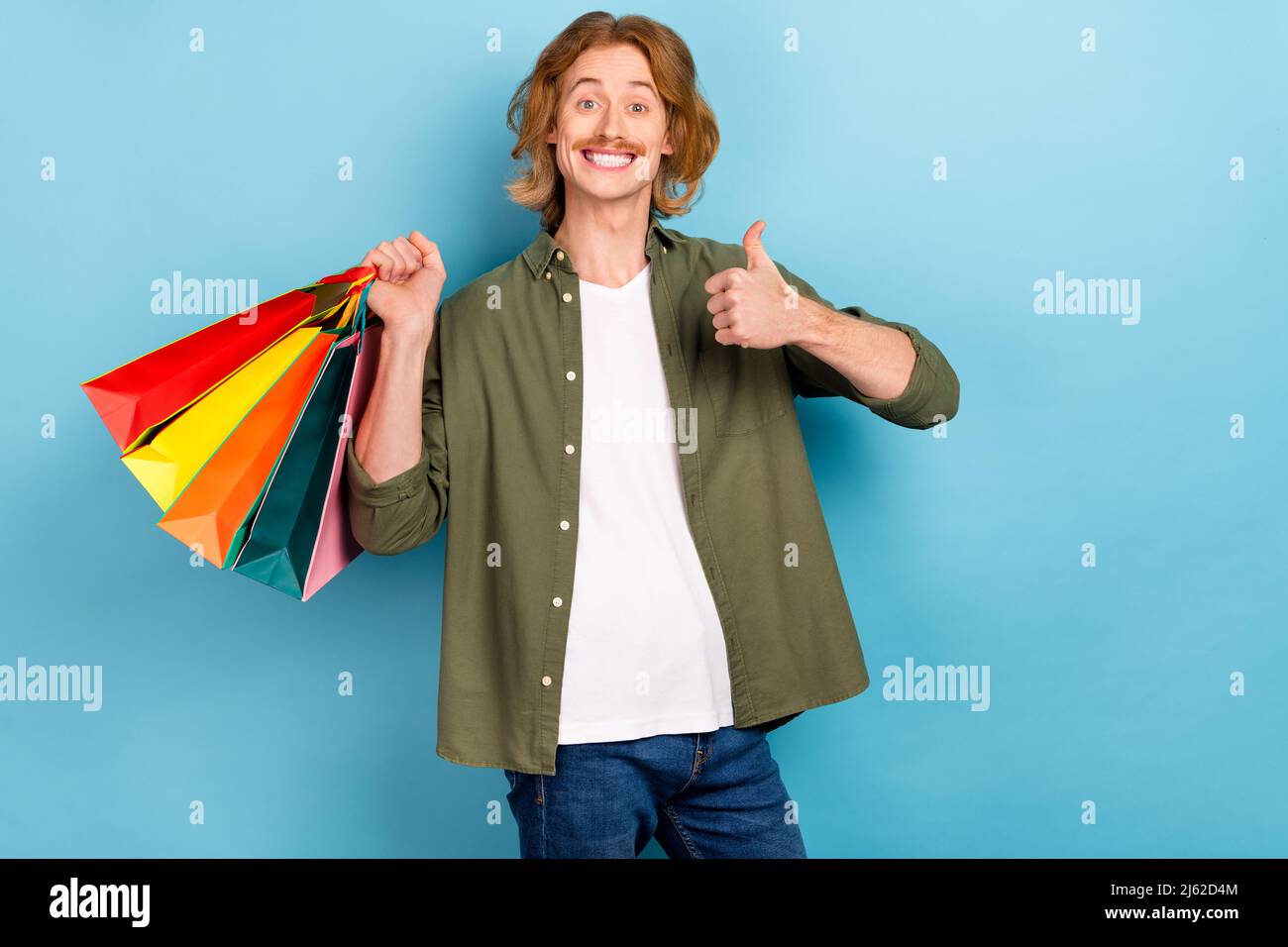 Portrait of attractive funky cheerful guy holding bags showing thumbup ...