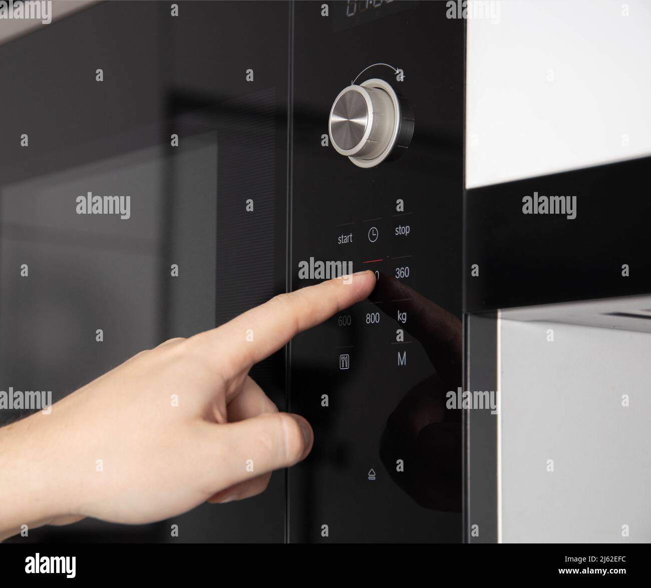 A man's hand presses the touch panel of a modern microwave oven to ...