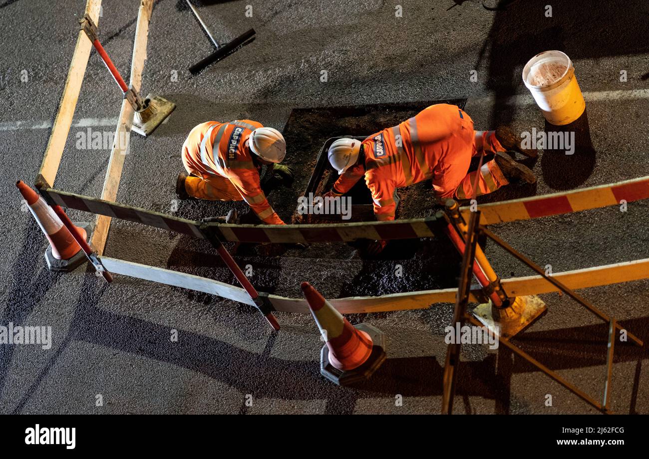 Night time roadworks, repairing a broken manhole cover in the road, in Hertfordshire, UK. Work ...