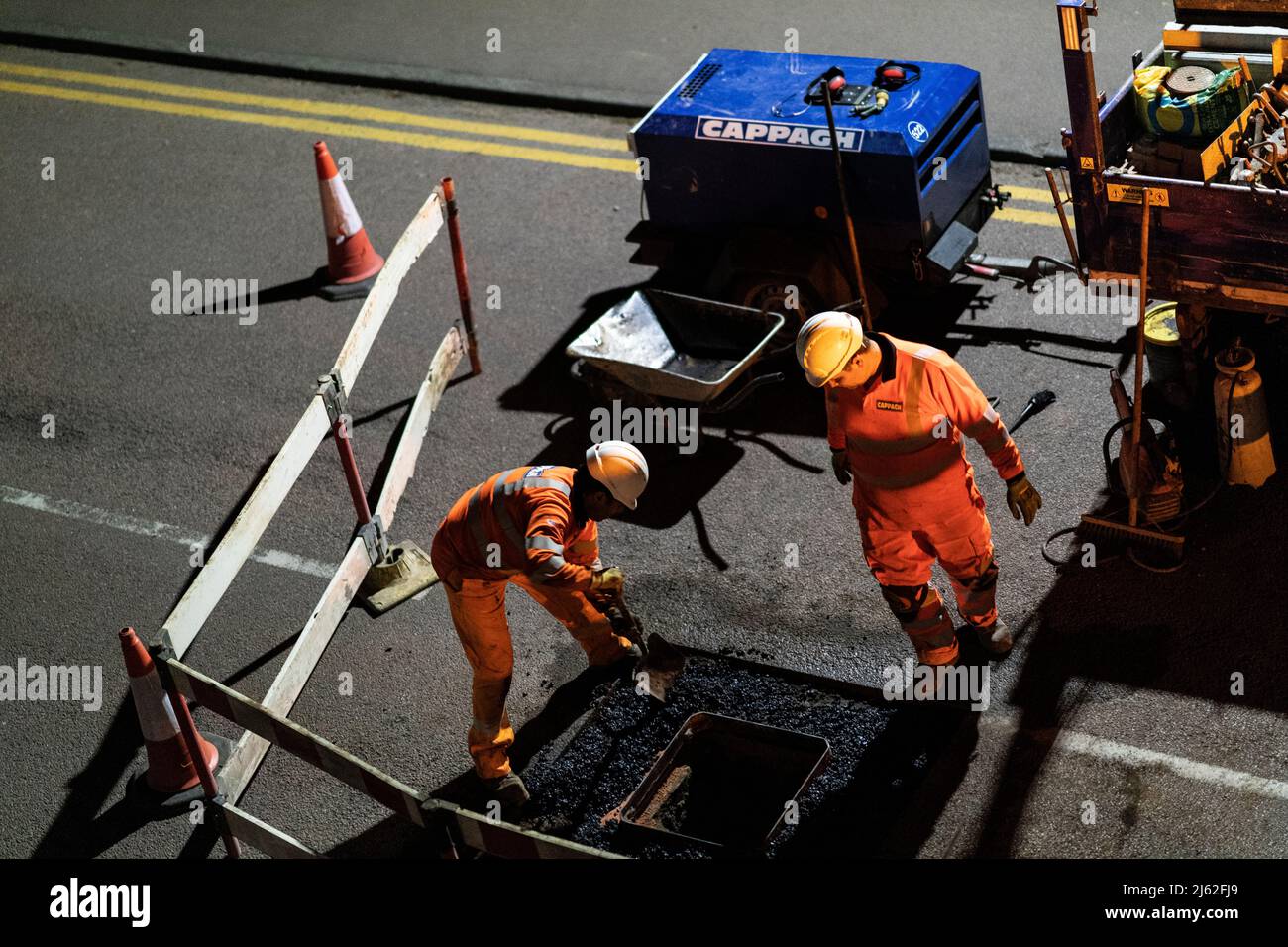 Night time roadworks, repairing a broken manhole cover in the road, in Hertfordshire, UK. Work ...
