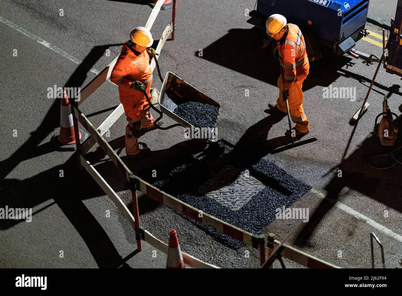 Night time roadworks, repairing a broken manhole cover in the road, in ...
