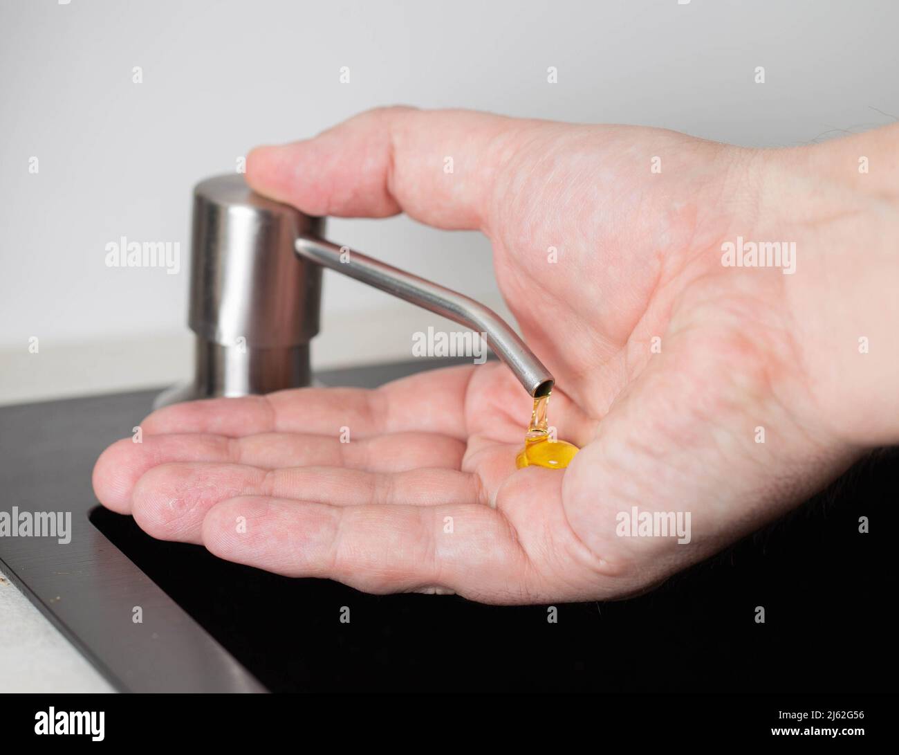 A person's hand presses on the dispenser in the sink with hand hygiene ...